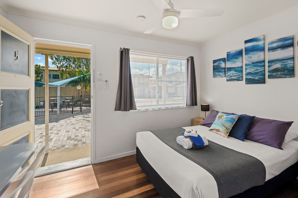 Quarto com cama, janela com cortinas, ventilador de teto e obras de arte na parede.