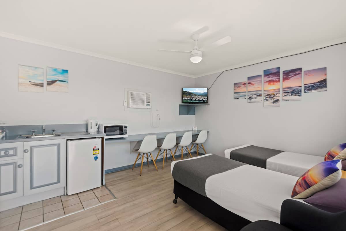 Quarto moderno com cama, escrivaninha e cozinha compacta.