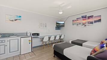 Quarto moderno com cama, escrivaninha e cozinha compacta.