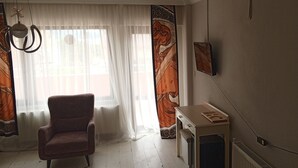 Um quarto com uma cadeira, uma mesa pequena, um radiador e uma janela com cortinas.