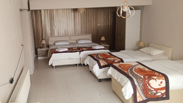 Quarto de hotel com televisão, duas camas, um sofá, uma mesinha de cabeceira com abajur e uma parede listrada.