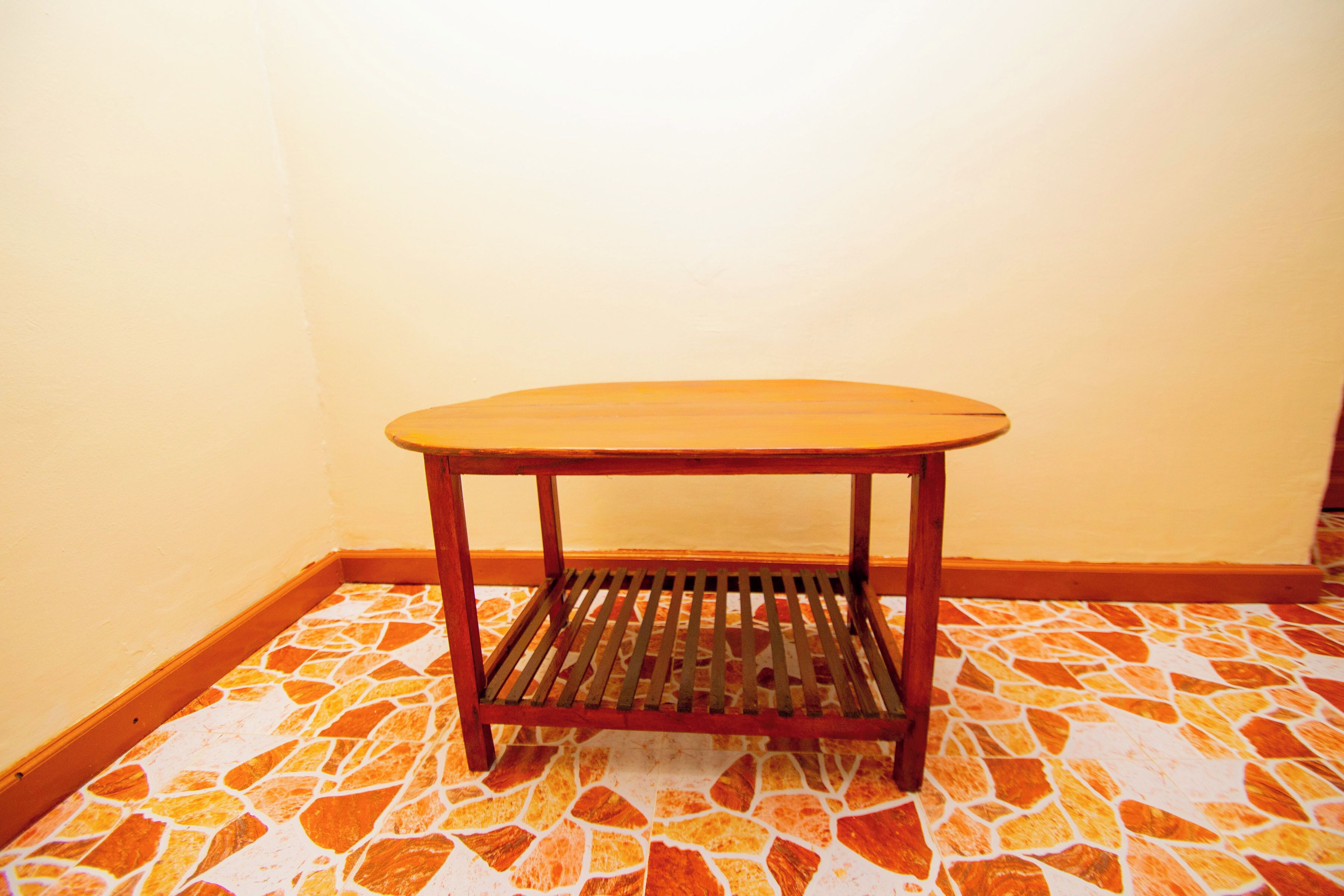 Uma mesa no canto com base ripada e tampo plano, sobre um chão estampado.