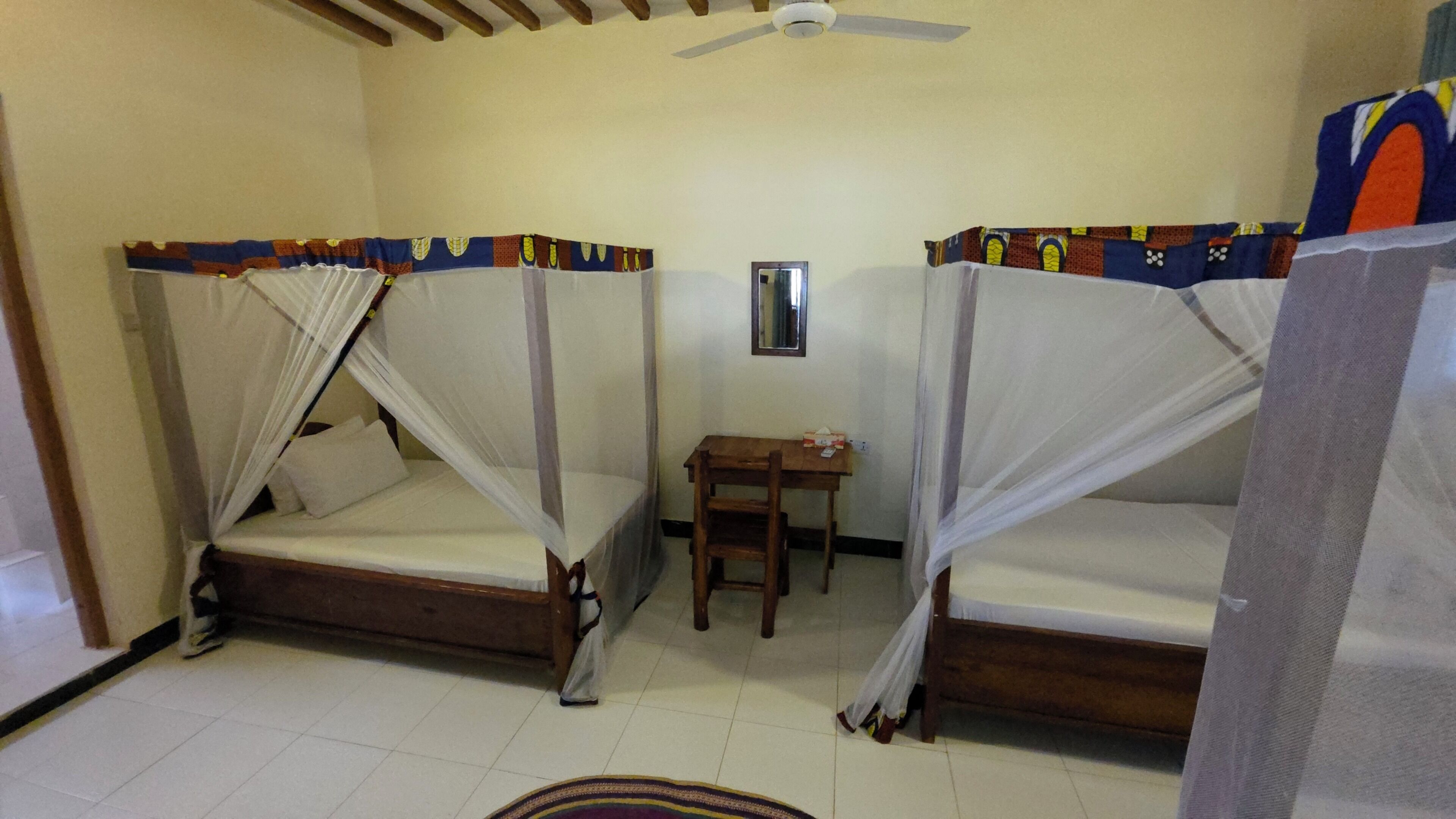 Quarto com duas camas de madeira, cada uma com dossel, uma mesa de madeira pequena e um ventilador de teto.