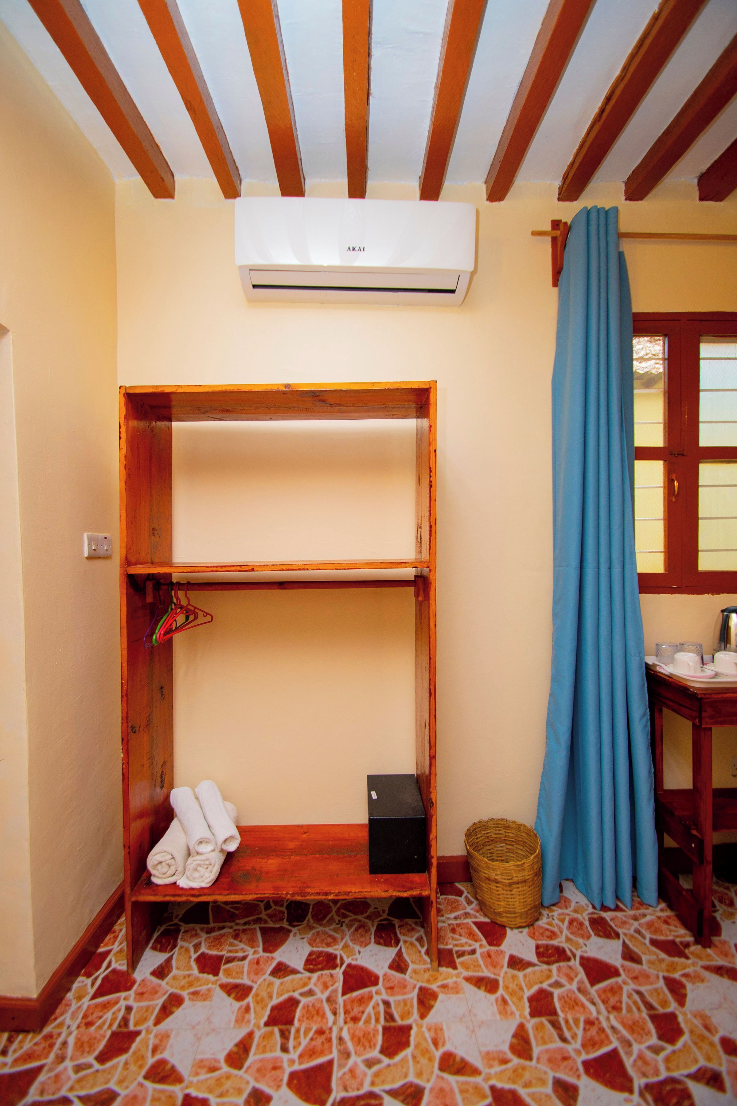 Um quarto com uma estante de madeira, ar condicionado fixado na parede, cortina azul e piso de azulejos.