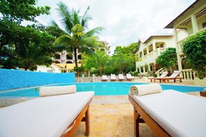 Uma área de piscina com espreguiçadeiras, piscina e um edifício com varandas.