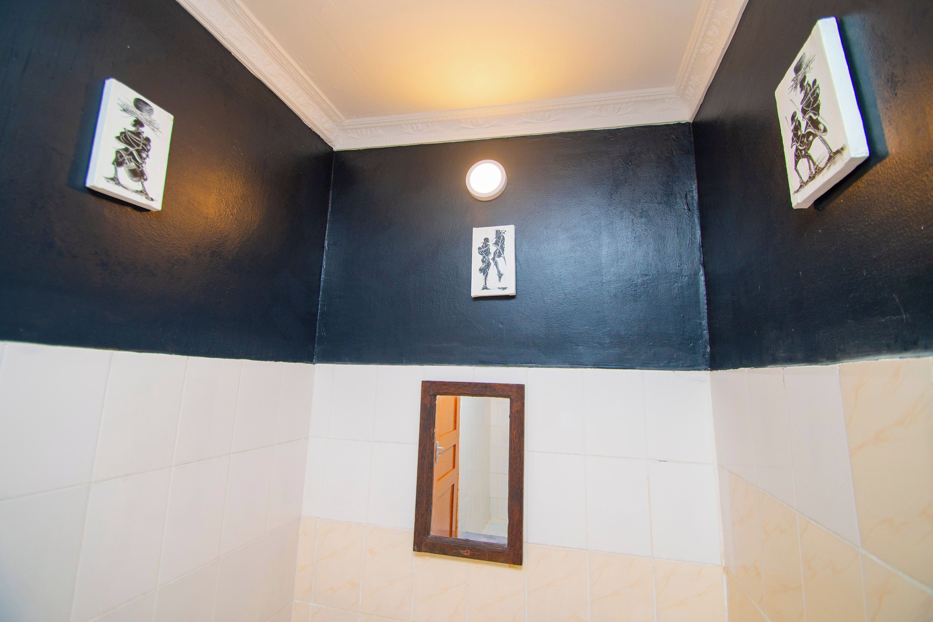Um banheiro com parede em azulejos preto e branco, um espelho pequeno e duas imagens emolduradas na parede.