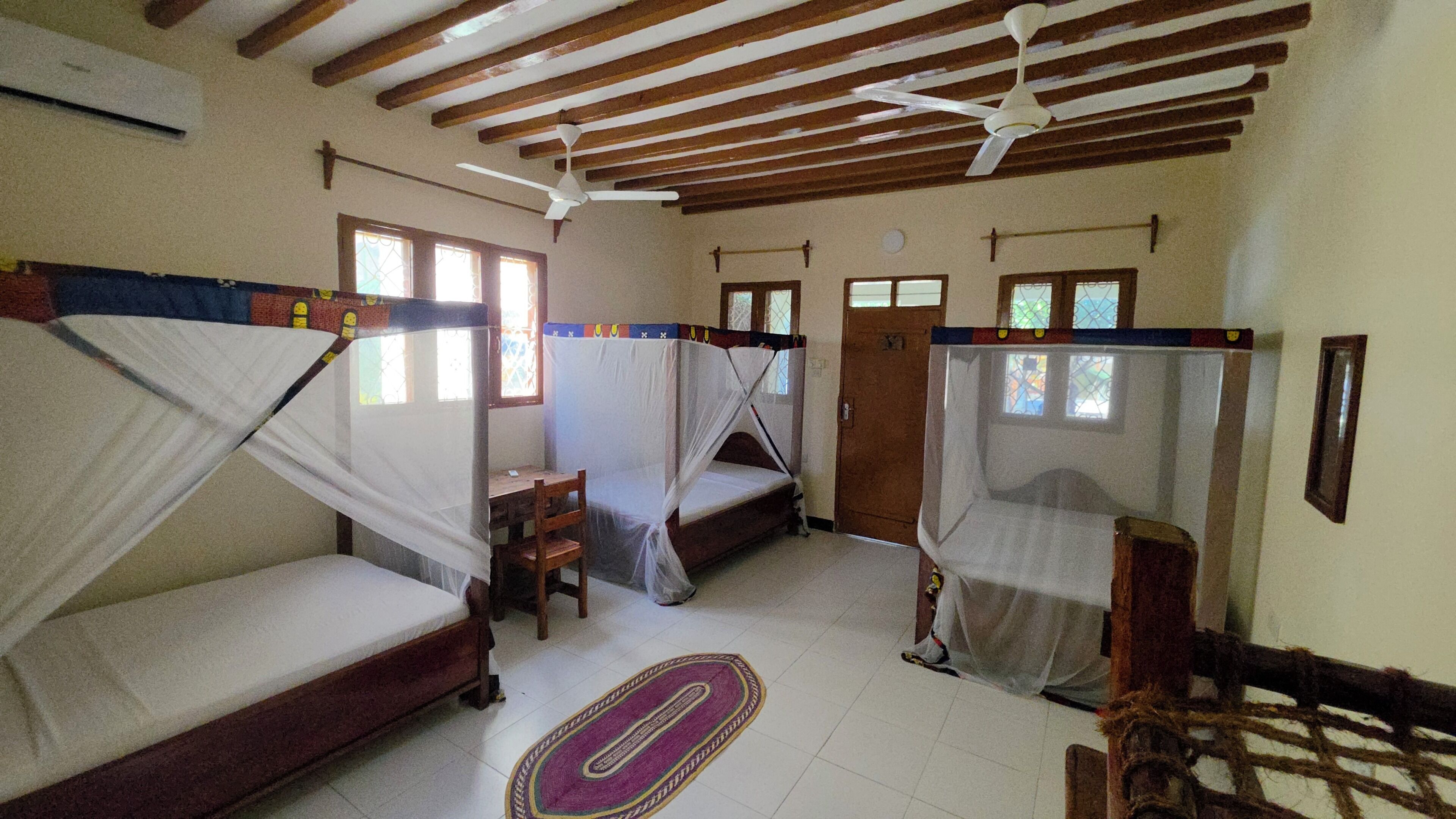 Quarto com duas camas, cada uma com mosquiteiro, teto de madeira e janela com vista.