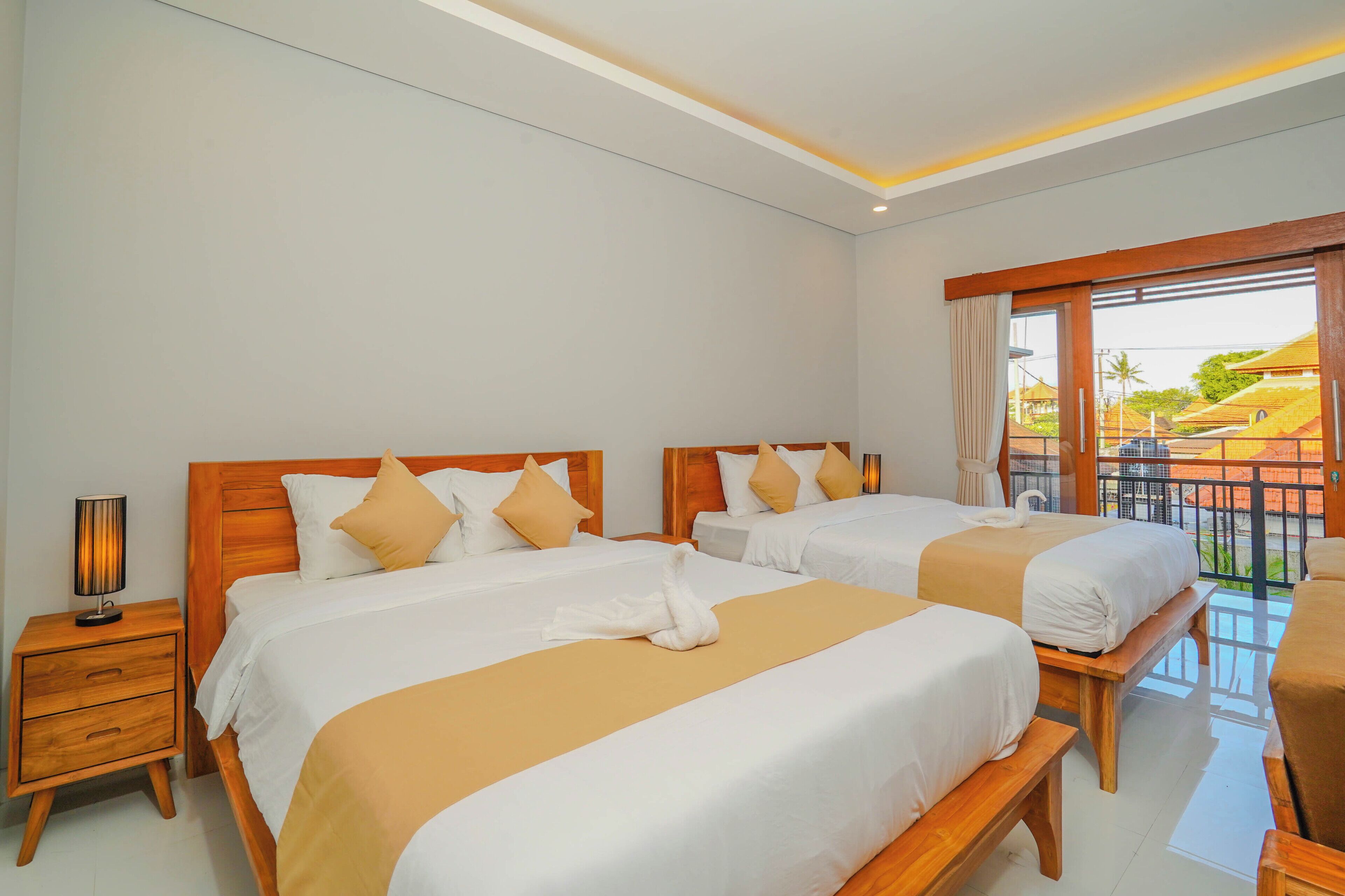 Quarto de hotel com duas camas, uma cabeceira de madeira, uma mesinha de cabeceira e vista para o exterior.