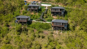 Um conjunto de quatro cabanas de madeira suspensas, com grades de metal, rodeado por vegetação densa.