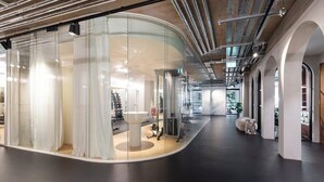 Um interior moderno com paredes de vidro curvo, um pedestal branco central e piso escuro.