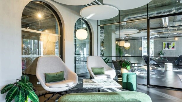 Um espaço de escritório moderno com assentos curvos, paredes de vidro e plantas em interior.