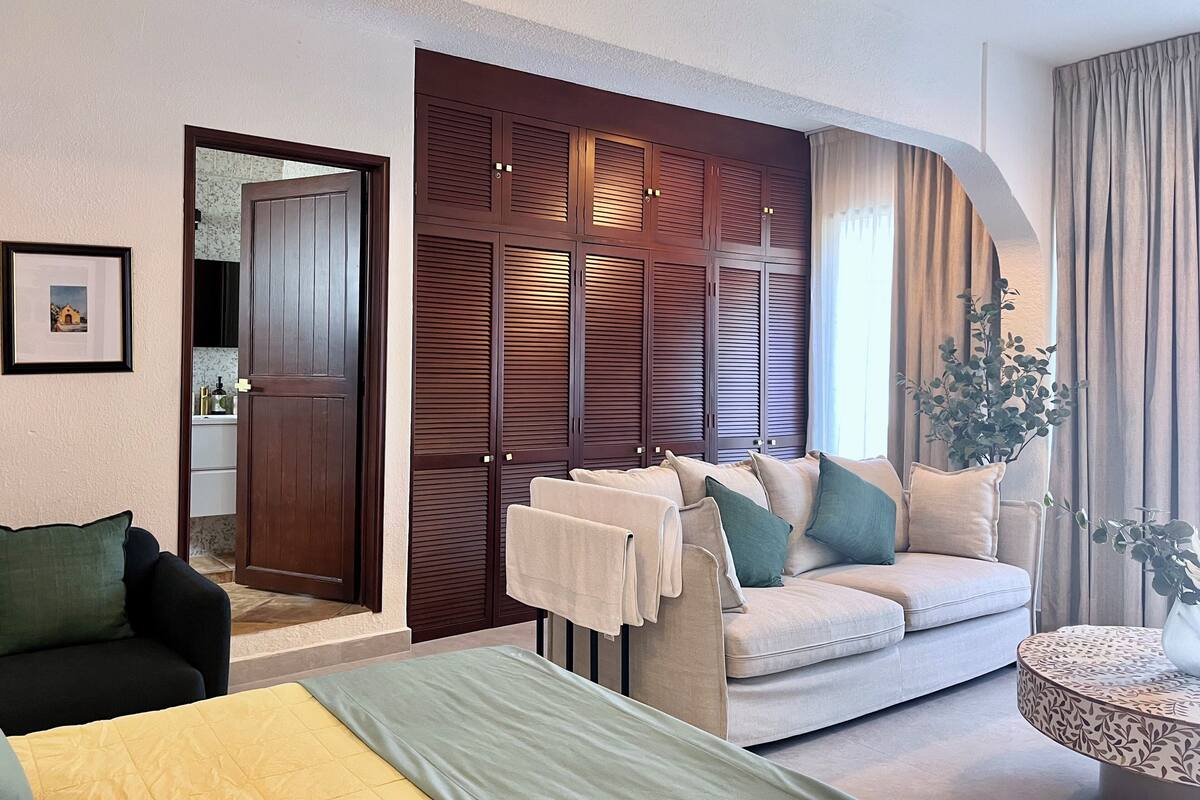 Quarto de hotel com cama, sofá, mesa de jantar, guarda-roupa de madeira e vista exterior.