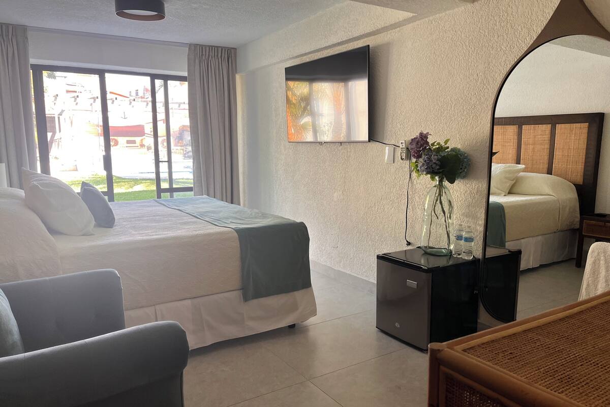 Quarto de hotel com cama, escrivaninha, cadeira, televisão e vista para o exterior.