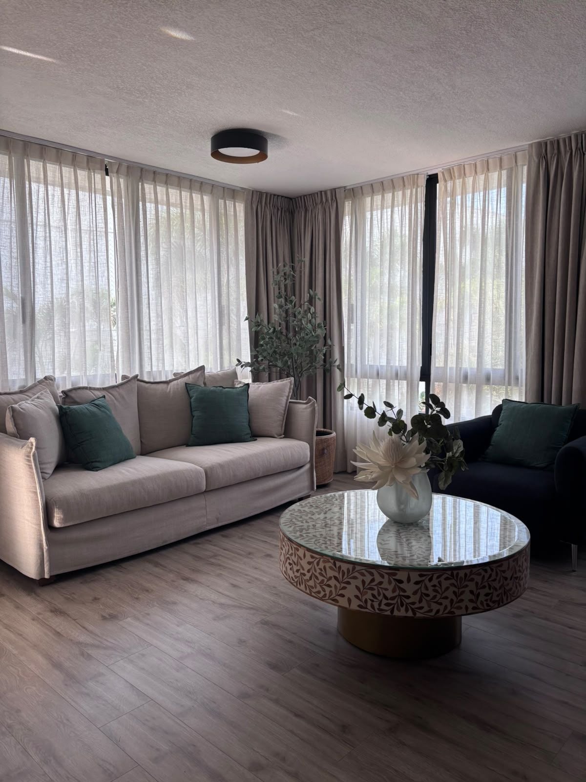 Uma sala de estar com um sofá bege, uma mesa de centro redonda e uma planta em vaso.