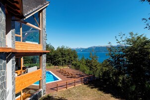 Um edifício moderno com fachada de pedra, deck de madeira e piscina.