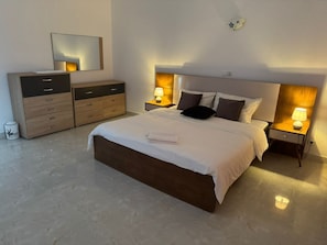 Quarto bem arrumado com cama grande, mesas de cabeceira com luminárias, cômoda e espelho na parede.