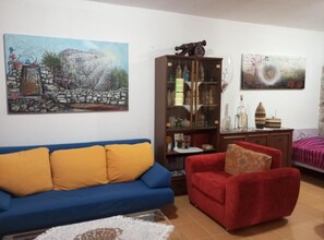 Uma sala de estar com um sofá azul, uma poltrona vermelha e uma estante de livros.