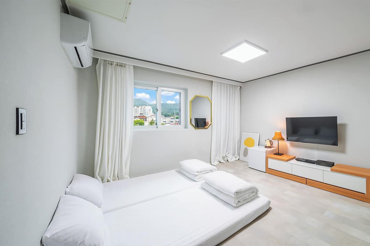 Quarto de hotel moderno com cama, televisão, uma mesinha e janela com cortinas.