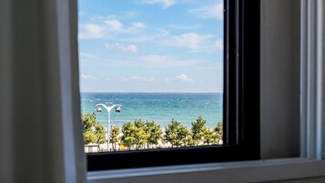 Vista pela janela de uma área costeira com um lampião, árvores e o oceano.