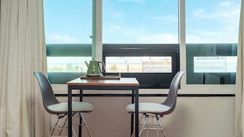 Quarto com uma mesa, duas cadeiras, uma janela com vista e uma chaleira sobre a mesa.