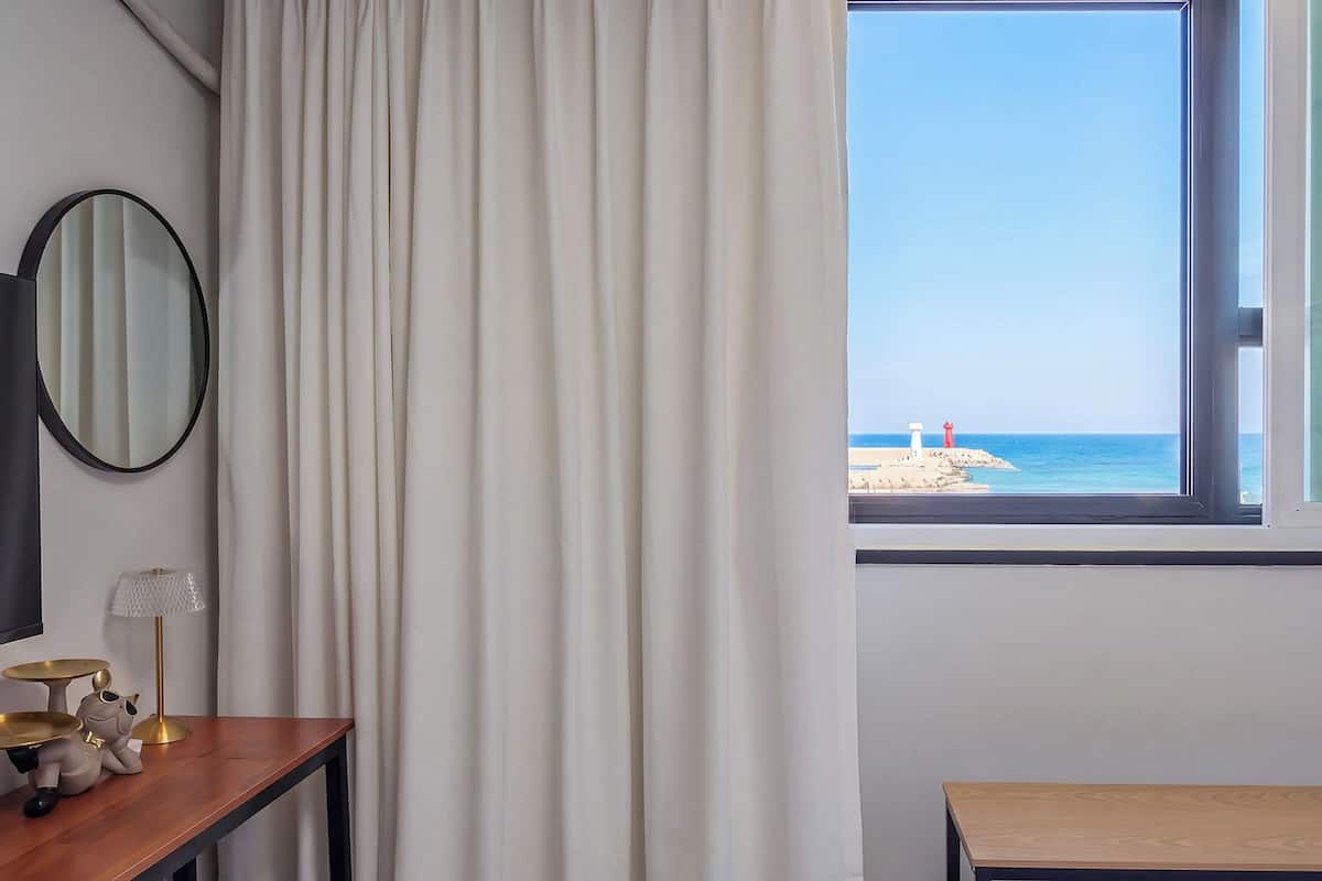 Quarto com vista para o mar, uma mesa de madeira, um espelho e um abajur.