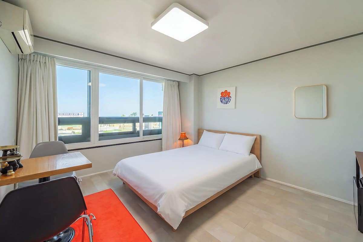 Quarto de hotel com cama, escrivaninha, cadeira e televisão.