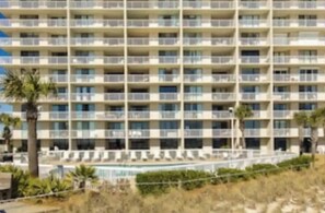 Um hotel com vários andares, varandas, piscina e vista para a praia.