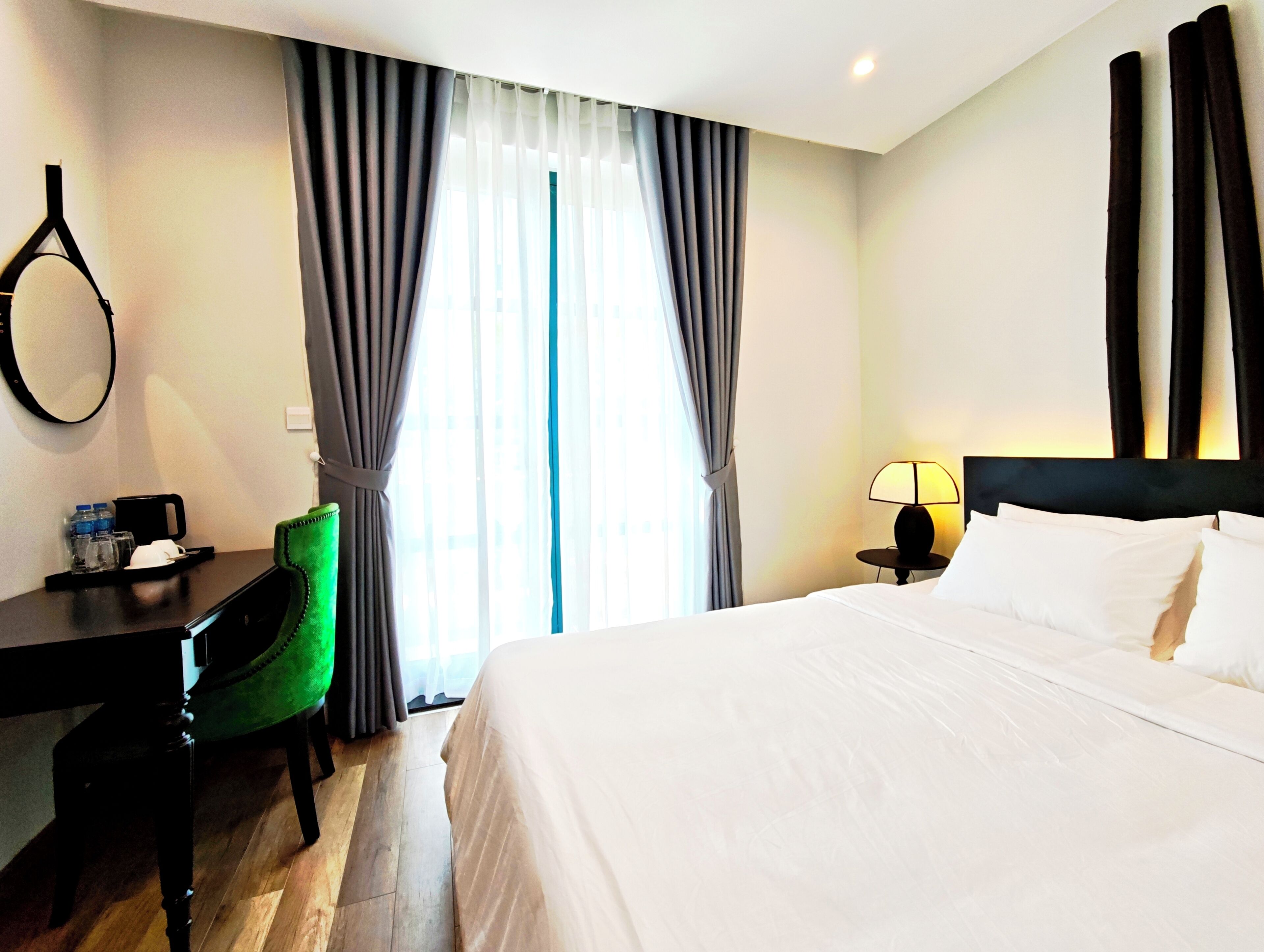 Quarto de hotel com cama, escrivaninha com cadeira, abajur e espelho na parede.