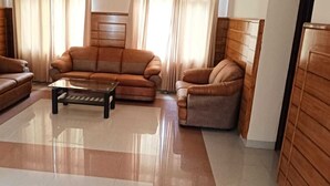 Uma sala de estar com um sofá, duas poltronas e uma mesa de centro de vidro.