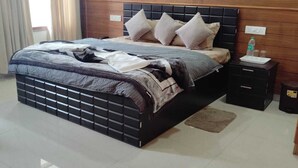 Quarto com cama, mesas de cabeceira, cabeceira de madeira e uma pequena mesa com uma garrafa e copos.