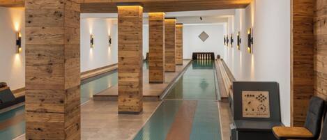 Um saguão de hotel com piscina, pilares de madeira e áreas de estar.
