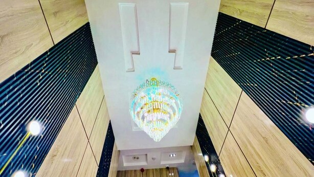 Um interior moderno com um lustre central, piso de madeira e escada com corrimão dourado.