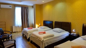 Quarto de hotel com duas camas, uma escrivaninha, uma cadeira e uma janela com cortinas.