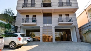 Hotel de dois andares com entrada central, varandas e carros estacionados na frente.