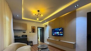 Uma sala de estar moderna com sofá, mesa de centro, TV na parede e área de cozinha ao fundo.