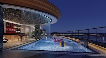 Uma área de piscina com bar e assentos, um flutuador de flamingo e vista para o mar.
