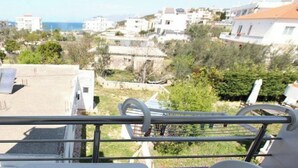 Uma varanda com mesa e cadeiras brancas, com vista para uma área residencial com casas e céu claro.