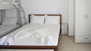 Uma cama de solteiro com cabeceira de madeira, mesa de cabeceira, guarda-roupa e uma cama beliche à esquerda.
