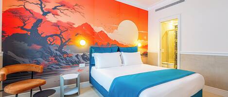 Quarto de hotel com um grande mural, uma cama com roupa de cama azul, uma cadeira de madeira e uma pequena mesa.