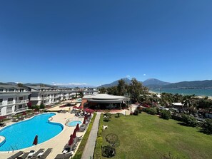 Resort com piscina, espreguiçadeiras e vista para o mar e montanhas.