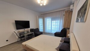 Quarto de hotel moderno com uma cama grande, uma escrivaninha com cadeira, televisão de tela plana e uma janela com cortinas.