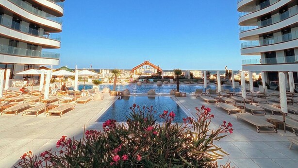 Área de piscina em resort, com várias espreguiçadeiras e uma piscina central.