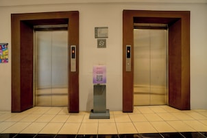 Duas elevadores com mostradores digitais, um aviso de proibido fumar e um código QR para confirmação de autoatendimento.