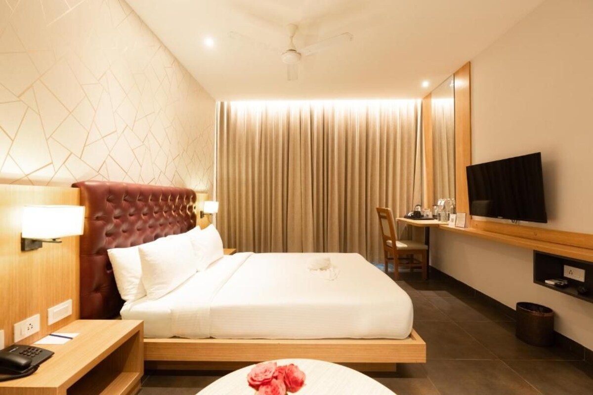 Quarto de hotel com cama, escrivaninha, cadeira, televisão e ventilador de teto.