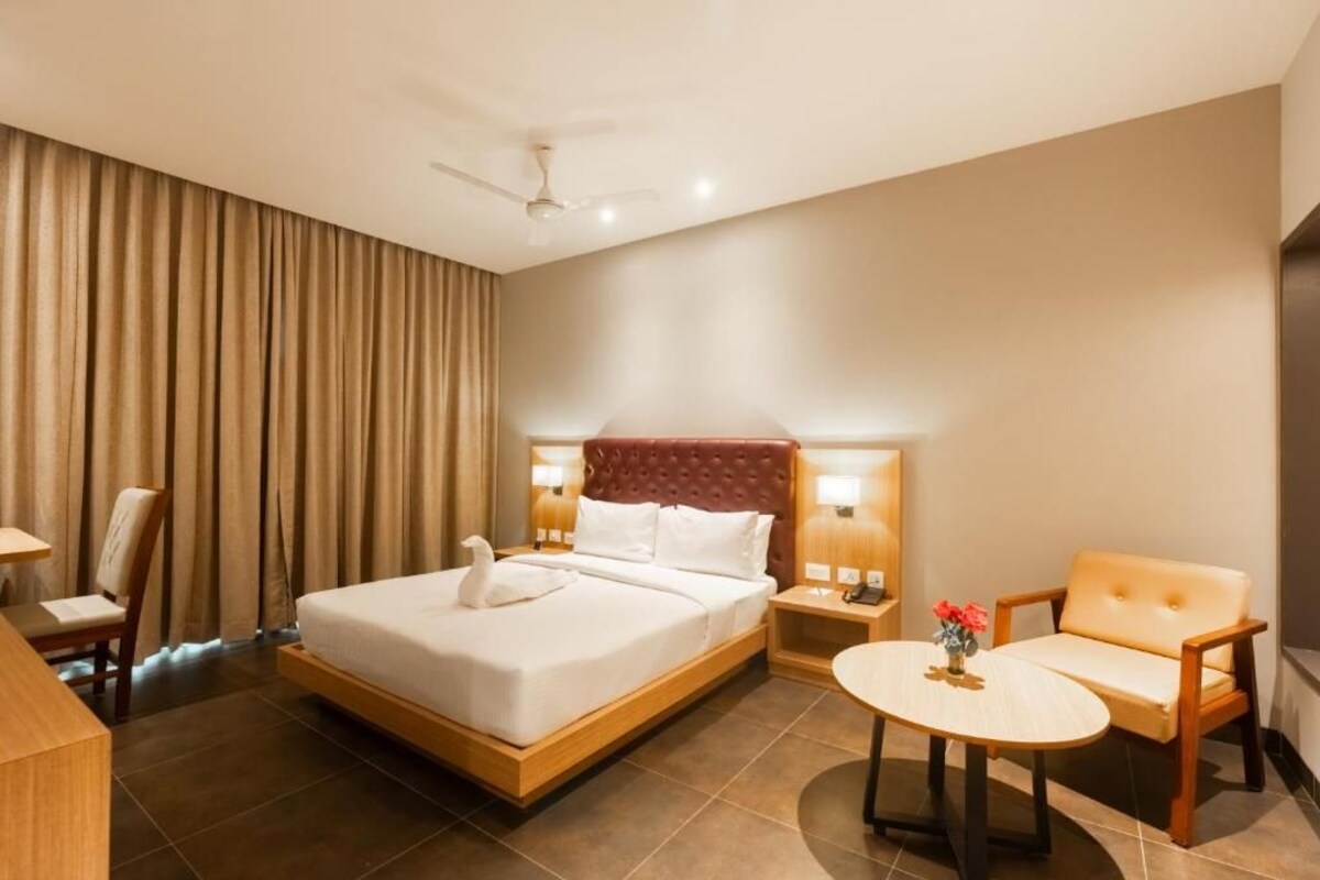 Quarto de hotel com cama, mesas de cabeceira, uma cadeira, uma mesa redonda e um ventilador de teto.
