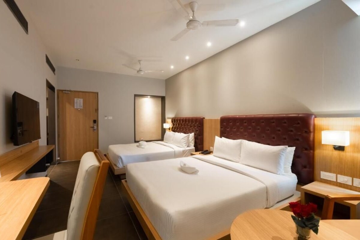 Quarto de hotel com duas camas, televisão, escrivaninha e uma cadeira.