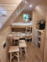 Uma cabana de madeira compacta com beliche, pequena cozinha e área de refeições.