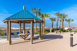 Um gazebo de madeira com telhado azul, palmeiras e um caminho pavimentado.