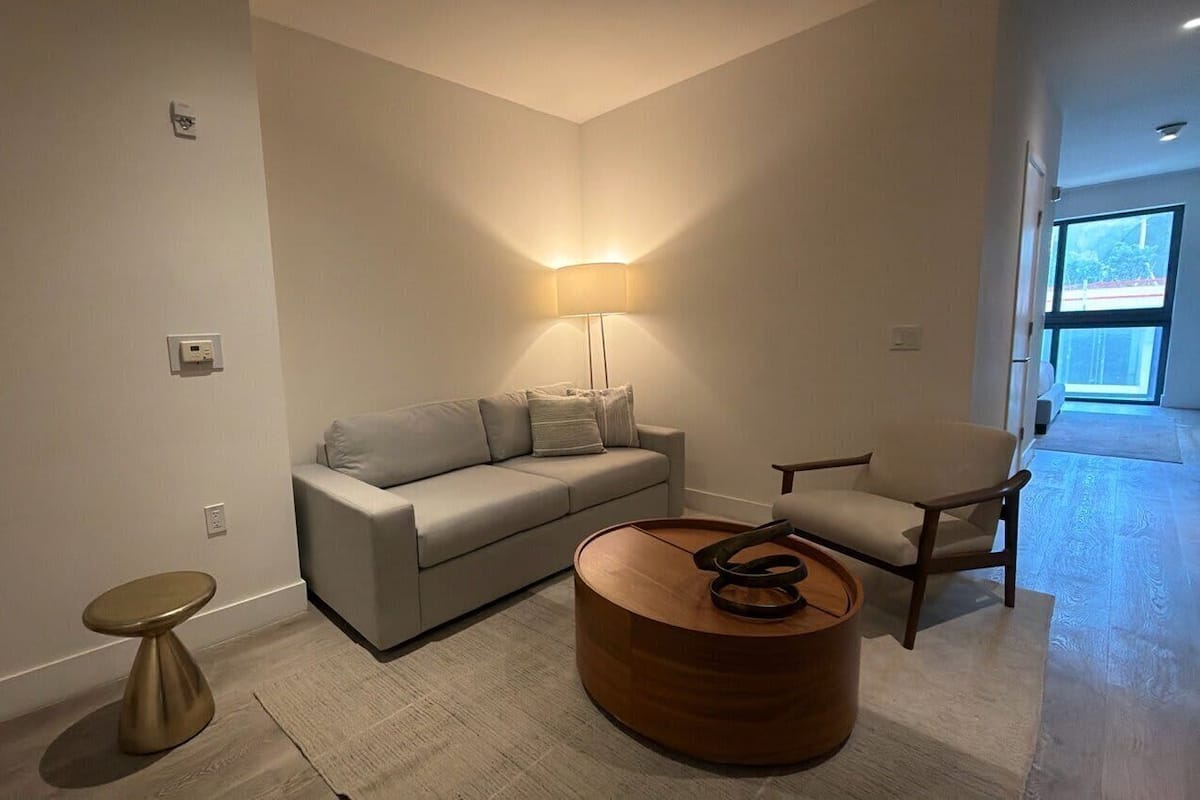 Uma sala de estar moderna com sofá, poltrona, mesa de centro redonda e abajur.