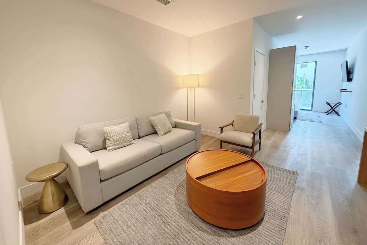 Uma sala de estar moderna com um sofá, poltrona, mesa de centro redonda e uma luminária.